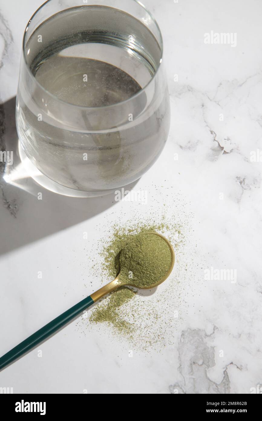 Green powder in spoon and glass of water. Concept of nutritional ...