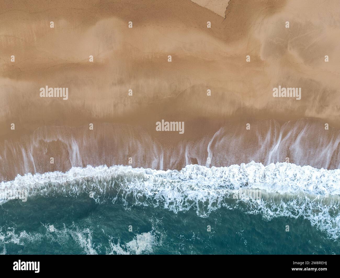 An aerial top view of ocean waves washing the sandy shore at a tranquil ...