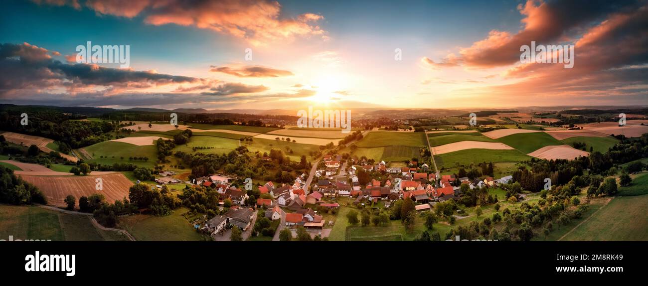 Aerial panorama of a village surrounded by fields at sunrise, with ...