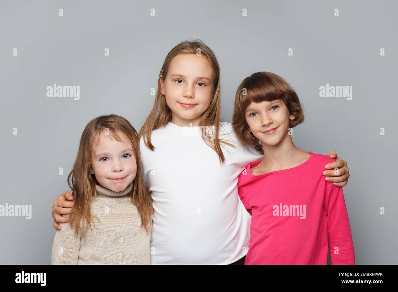 Happy small girls children embracing against grey studio wall ...