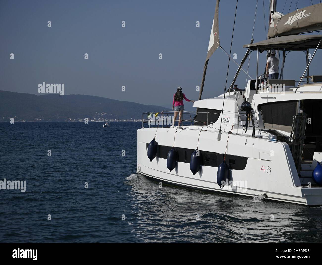 Scenic seascape with a young girl on the stern of a Catamaran sailing ...