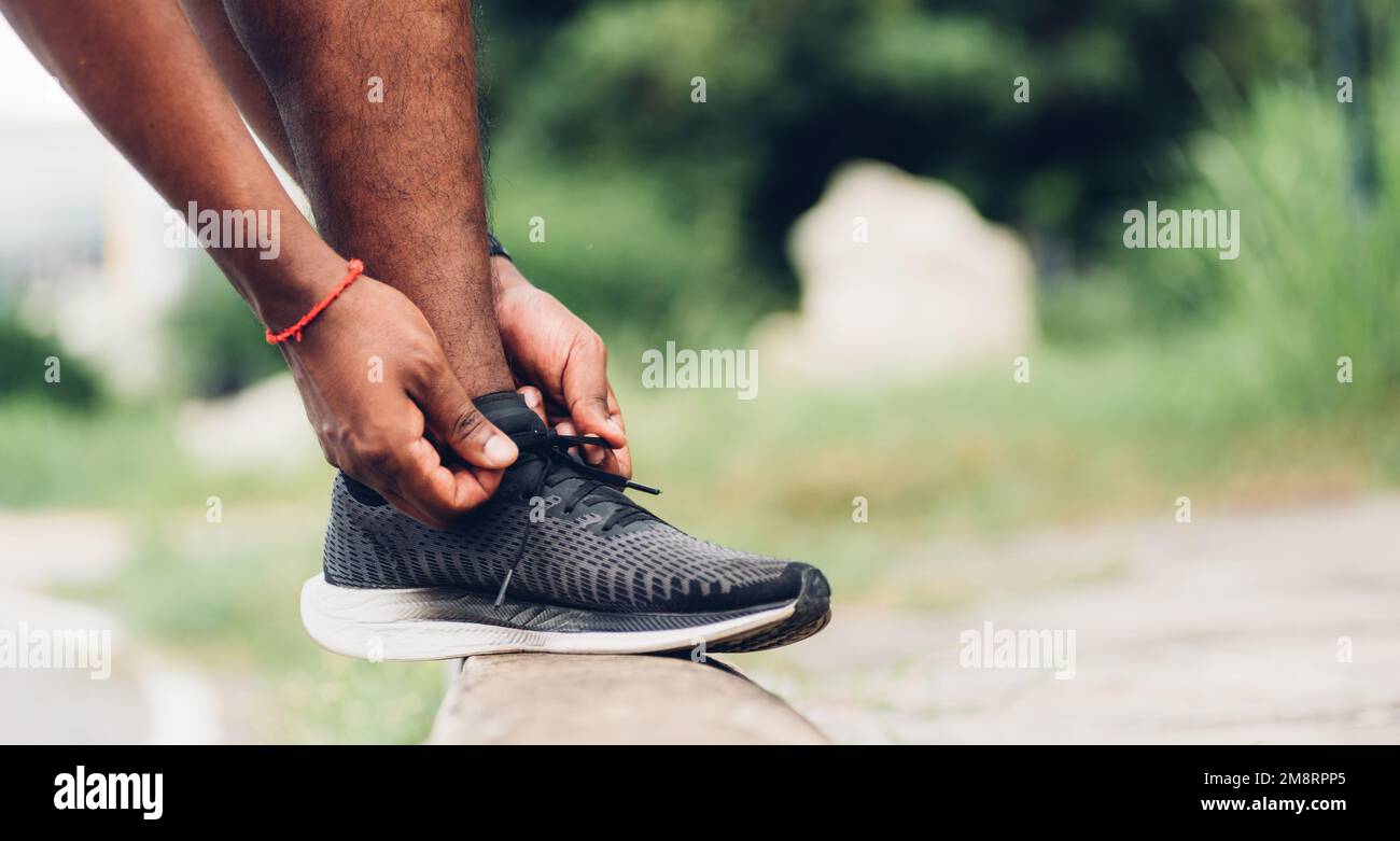 runner black man wear watch stand step on the footpath trying shoelace ...