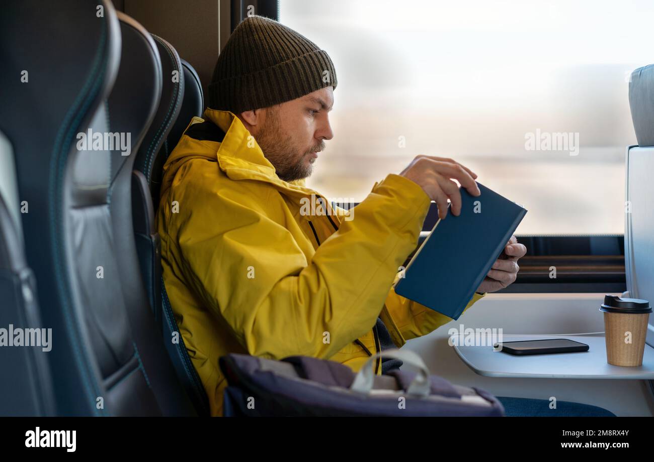 Bearded man in winter yellow jacket and hat reading book while ...