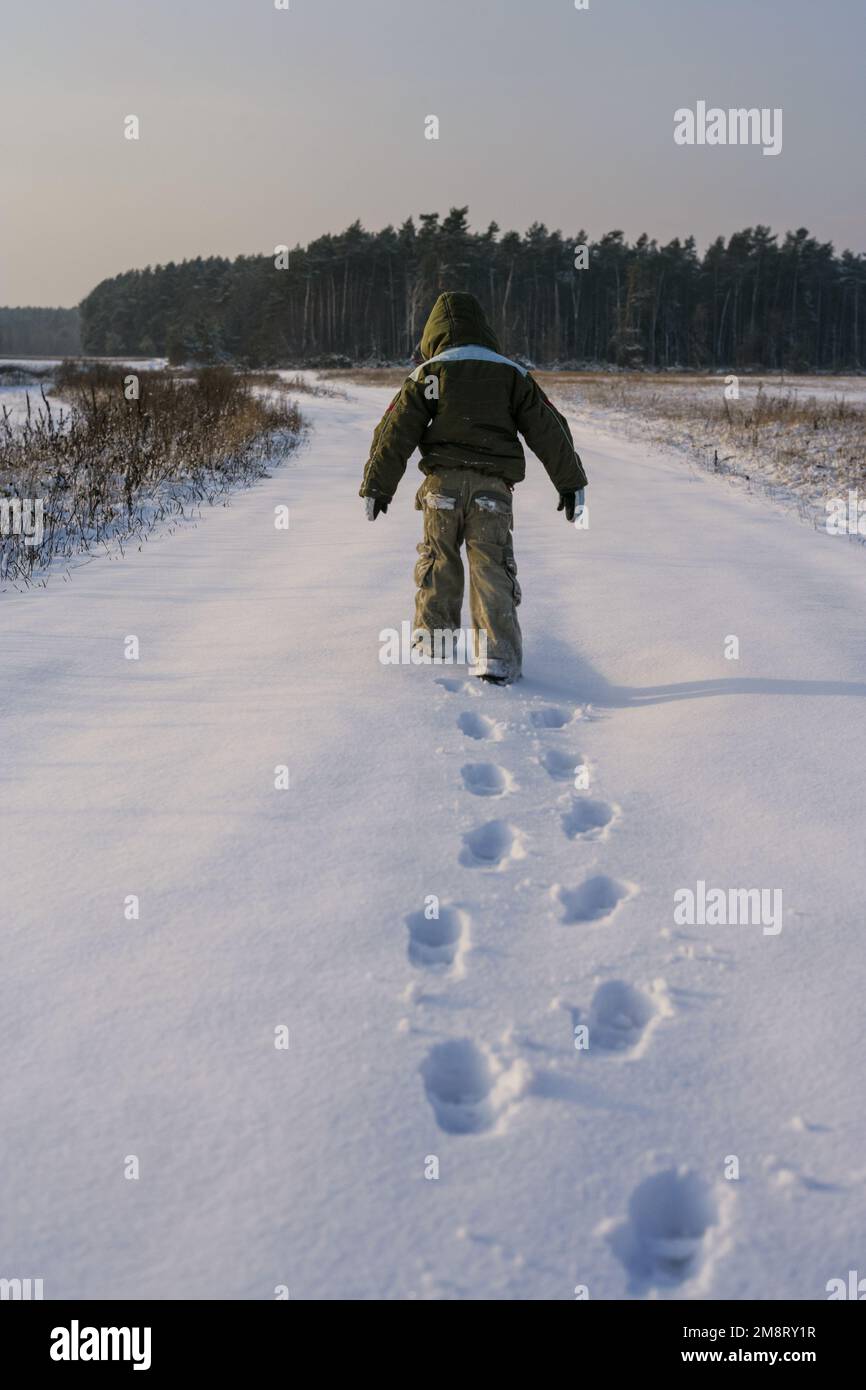 Little boy back view walking through the nature. Footprints in the snow ...