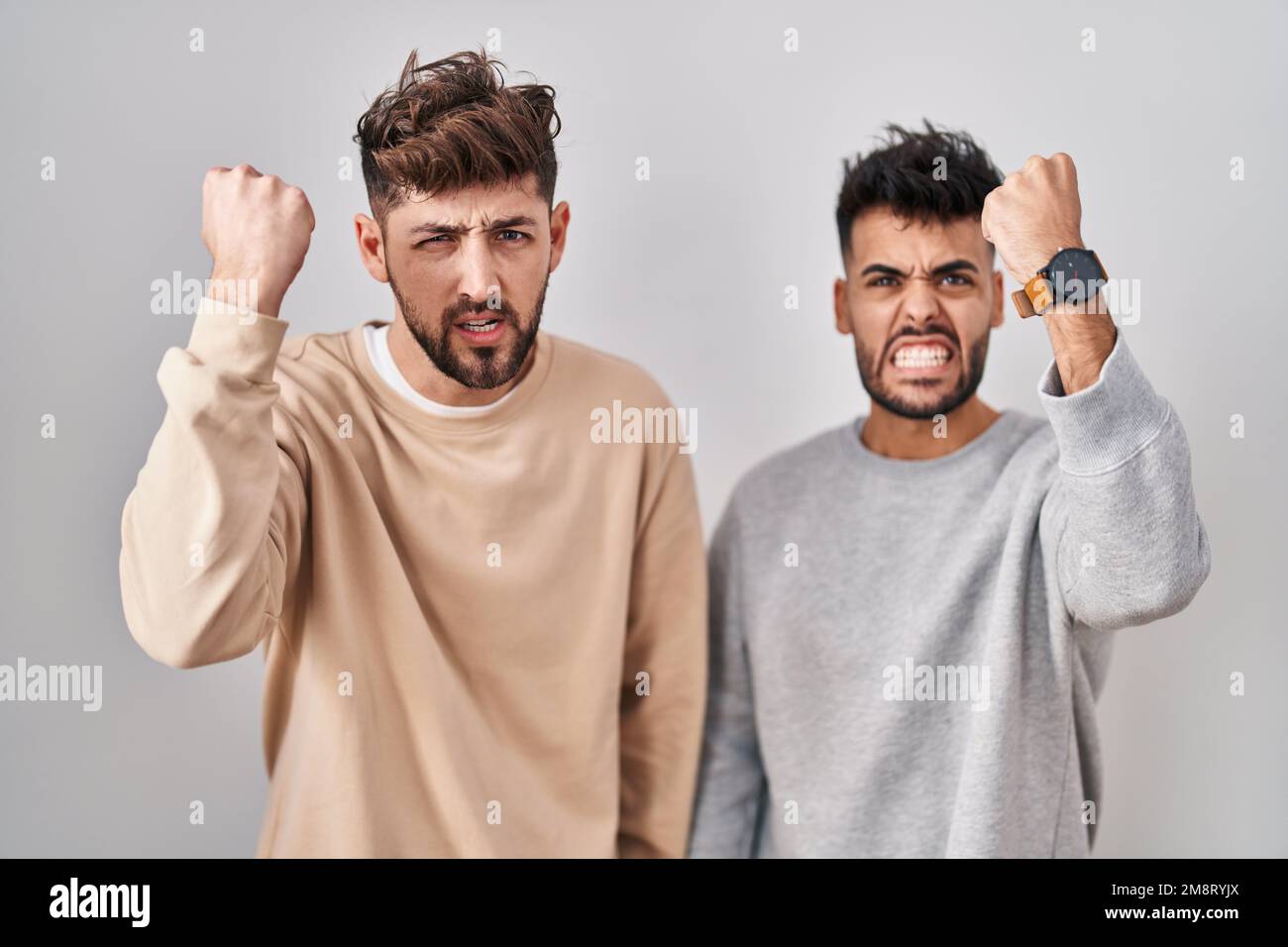 Young homosexual couple standing over white background angry and mad ...