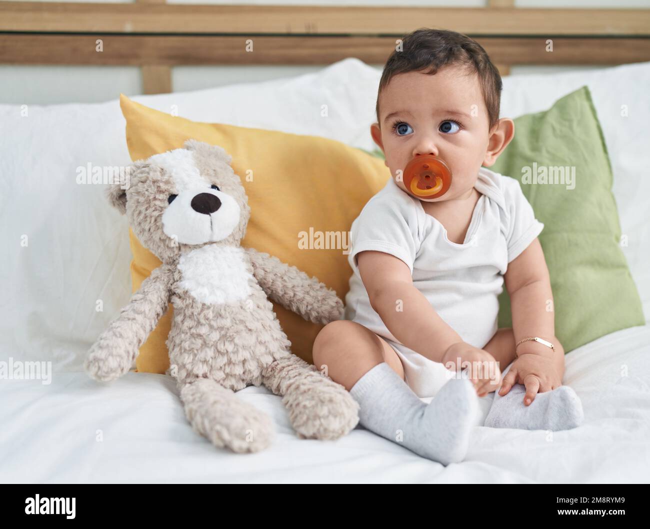 Adorable hispanic baby sucking pacifier sitting on bed at bedroom Stock ...