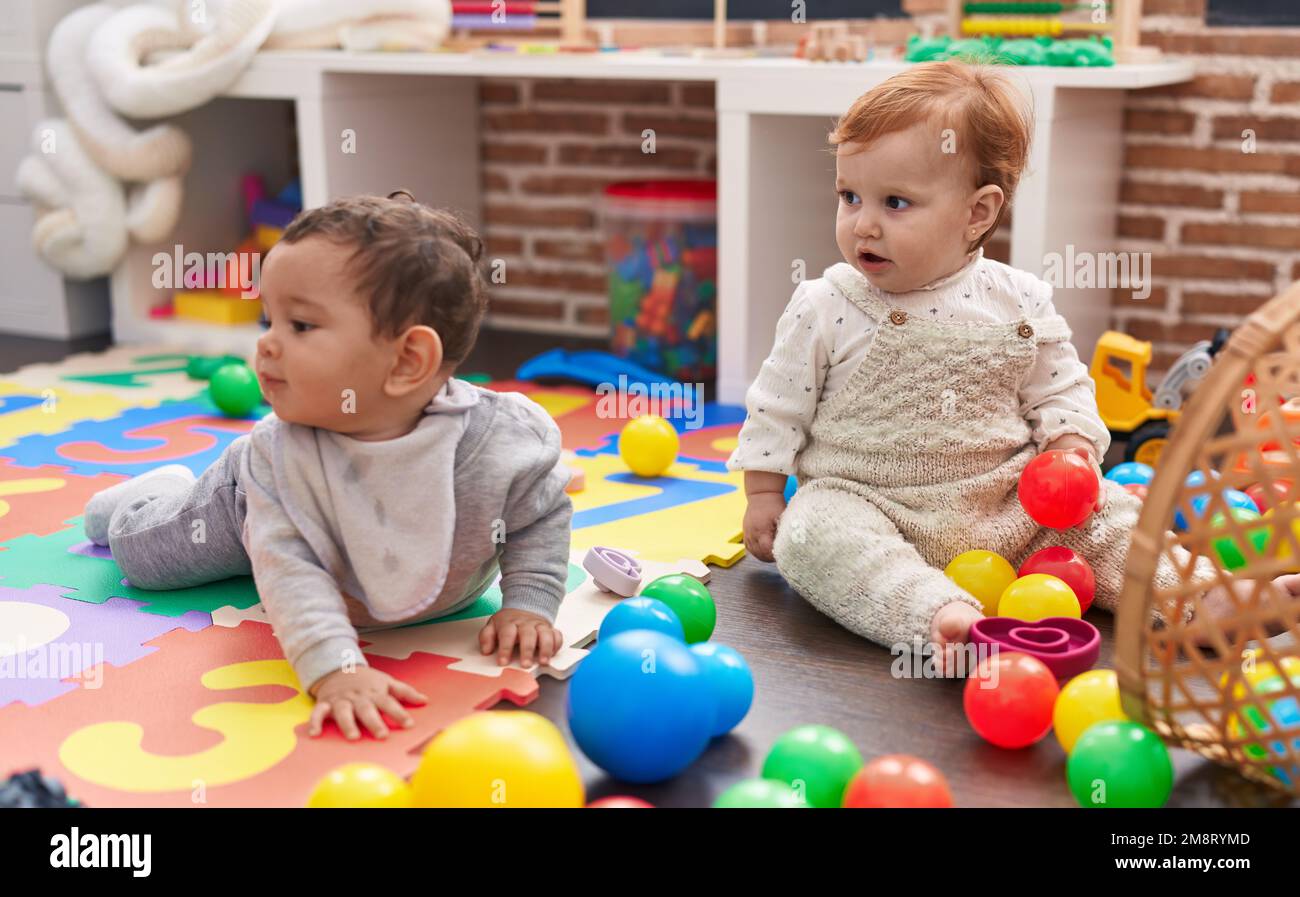 Two adorable babies playing with balls sitting on floor at kindergarten ...