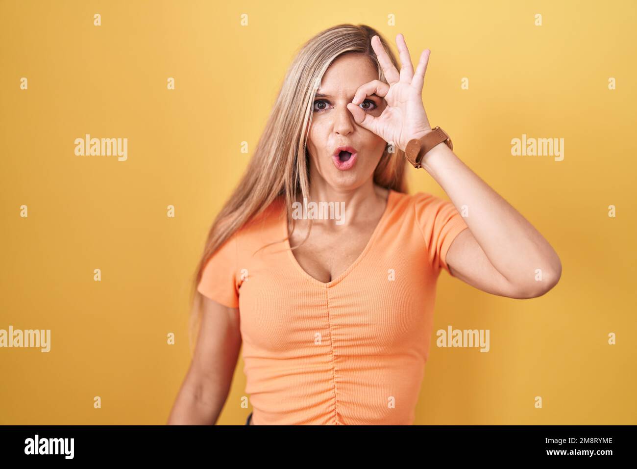 Young woman standing over yellow background doing ok gesture shocked ...
