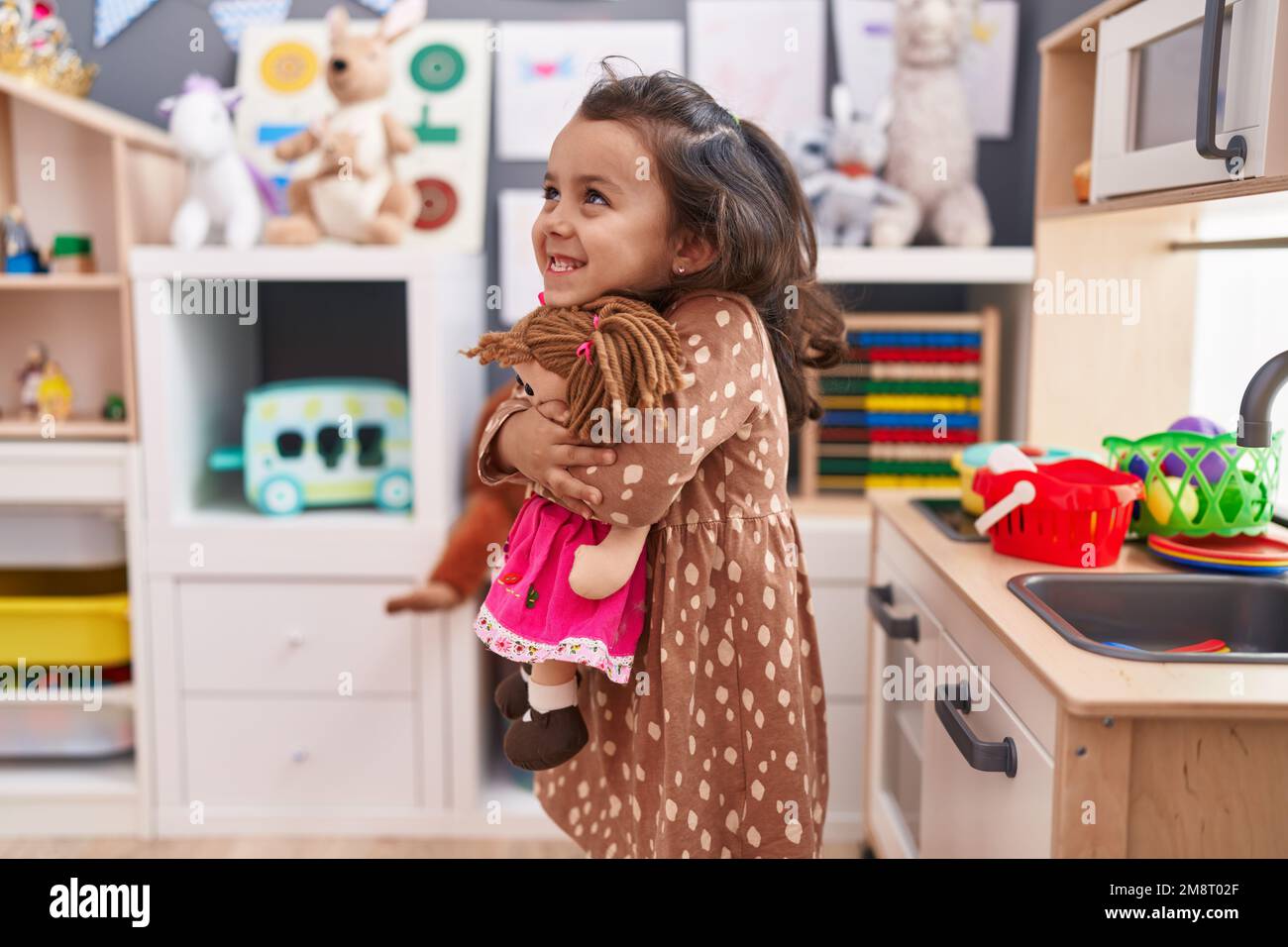 Adorable hispanic girl hugging doll standing at kindergarten Stock ...