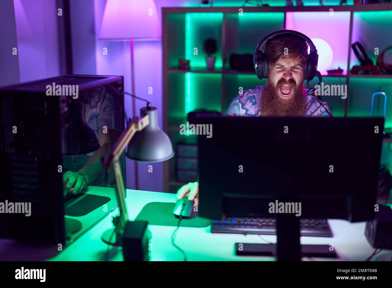 Young redhead man streamer playing video game using computer at gaming ...