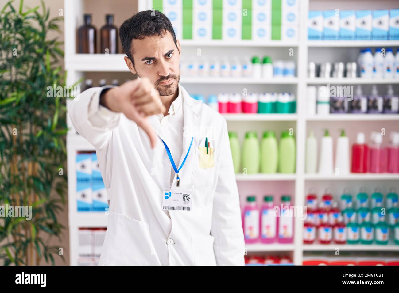 Handsome hispanic man working at pharmacy drugstore looking unhappy and ...