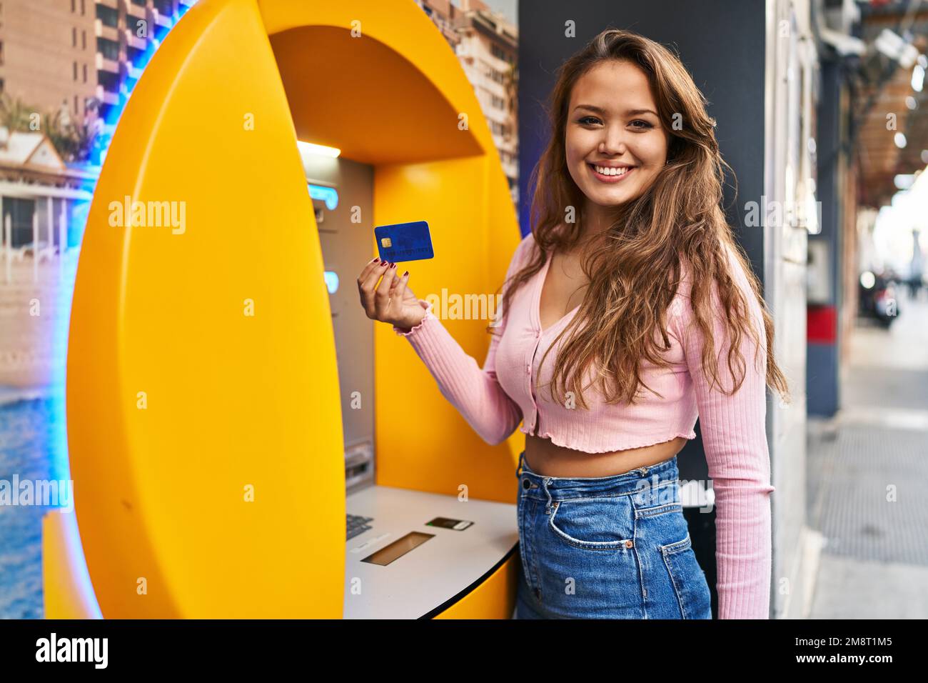 Young hispanic woman taking cash from atm with credit card looking ...