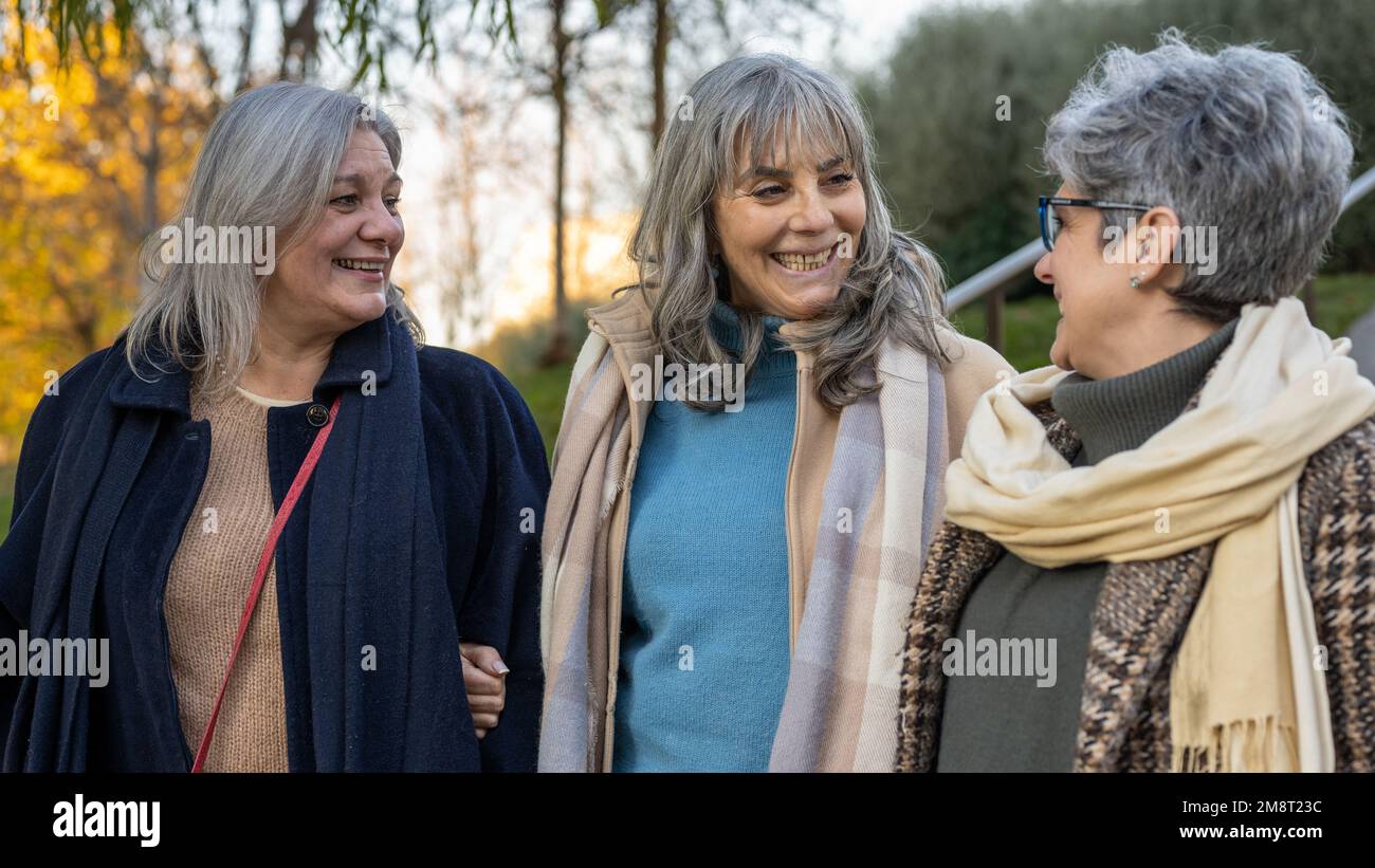 Three mature seniorn women friends walking outside and chatting, happy ...