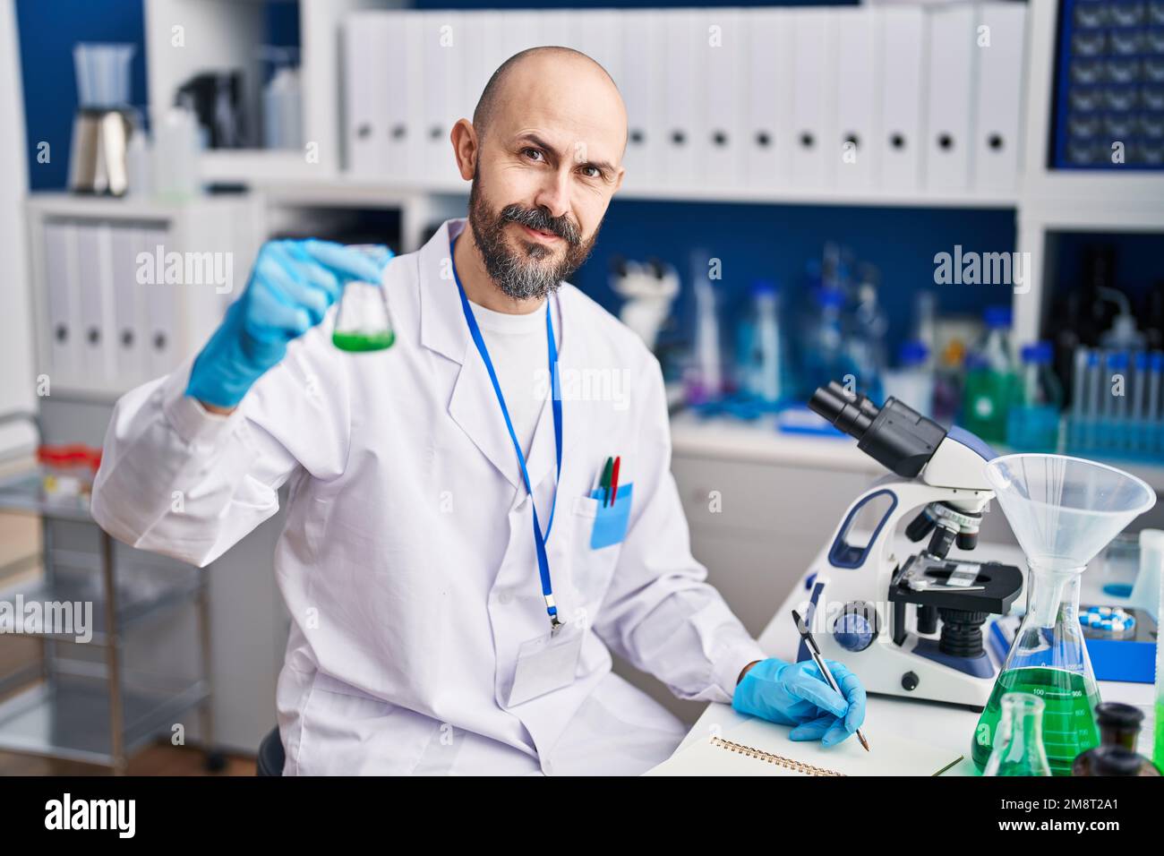 Young bald man scientist holding test tube writing on notebook at ...