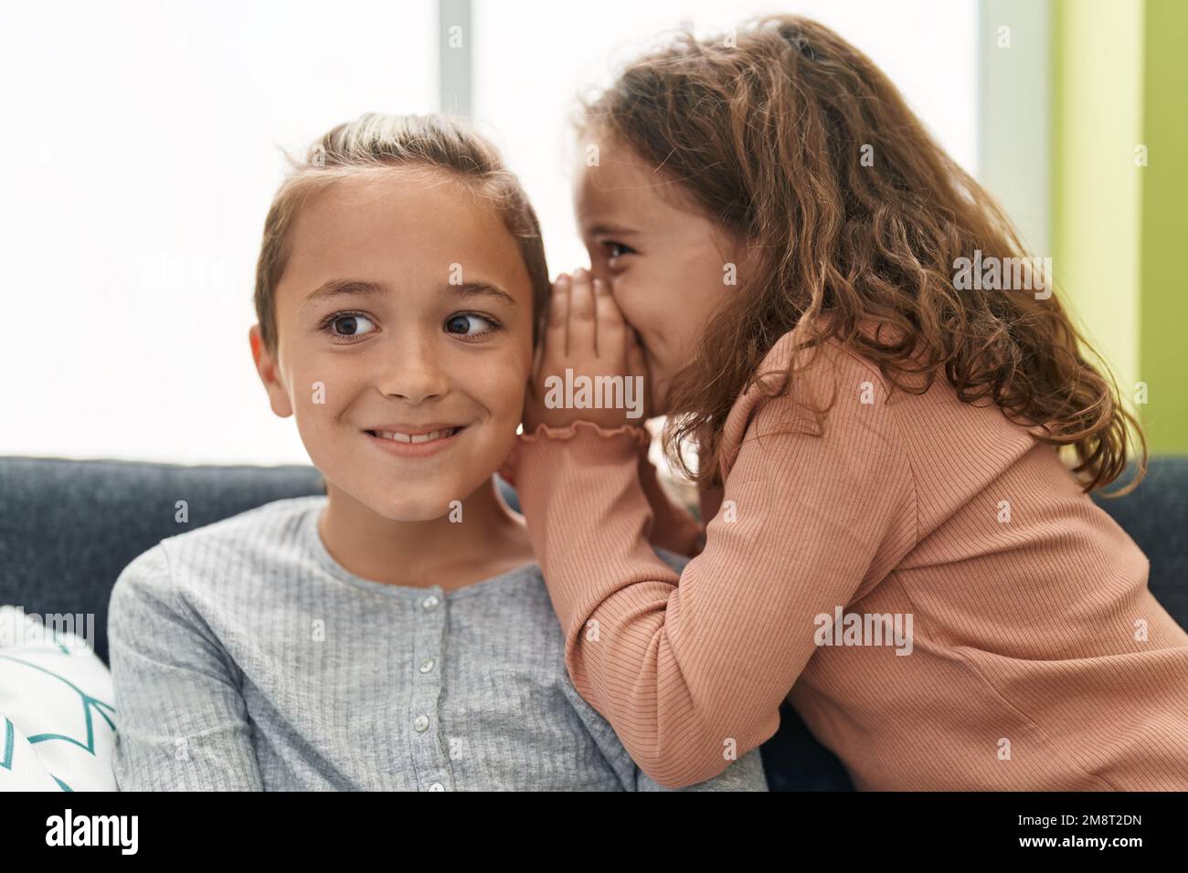 Two kids telling secret sitting on sofa at home Stock Photo - Alamy