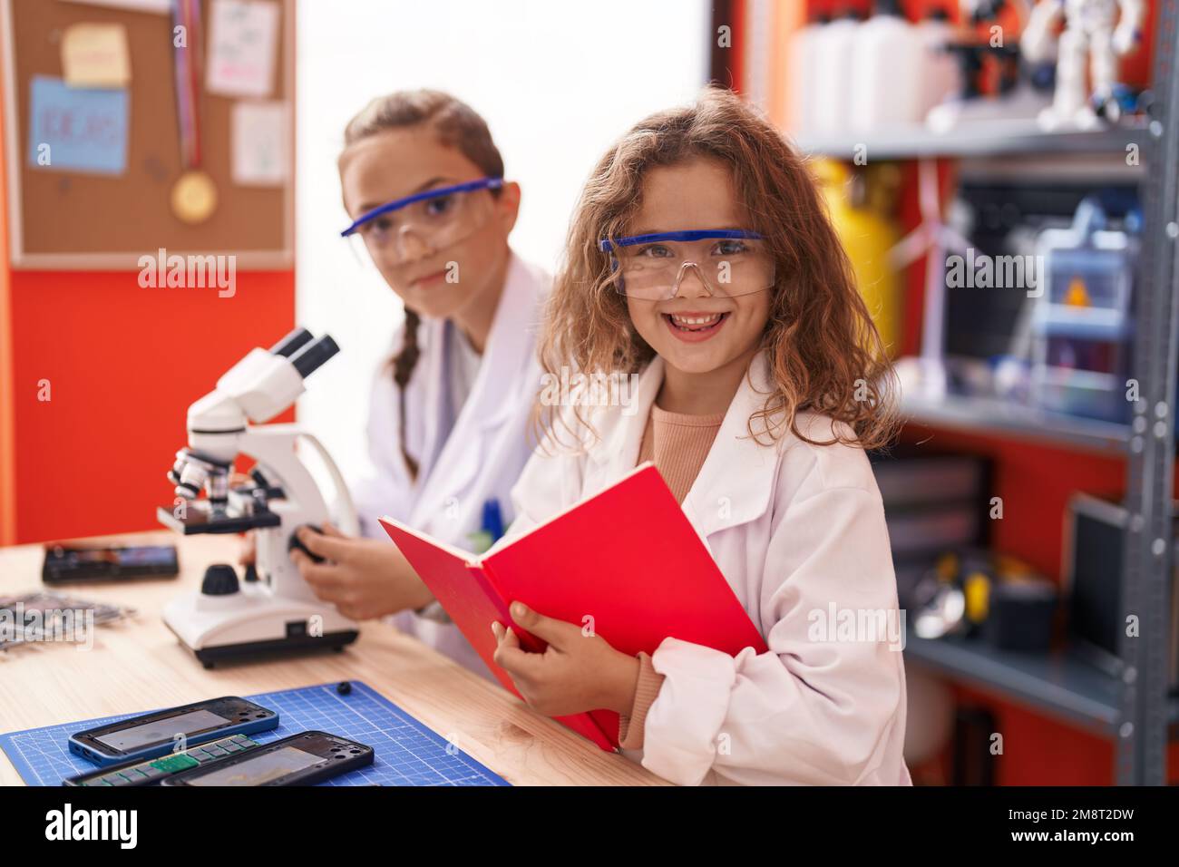 Two kids students using microscope writing on notebook at laboratory ...