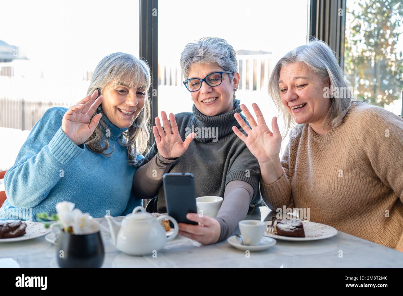 Three female elder friends using smart phone and social network to send video message and having ...