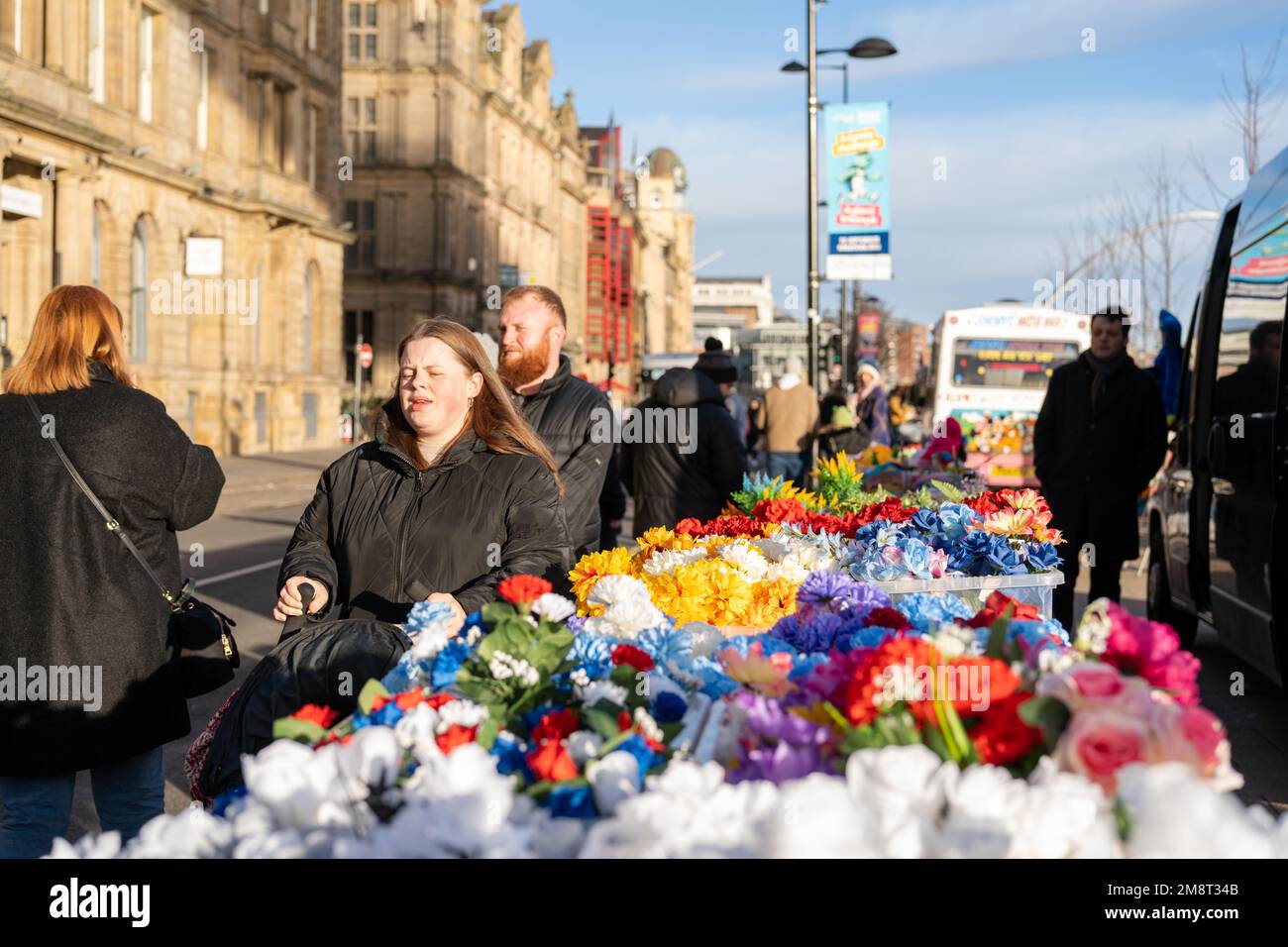 People walking past a stall of colourful synthetic flowers at the ...
