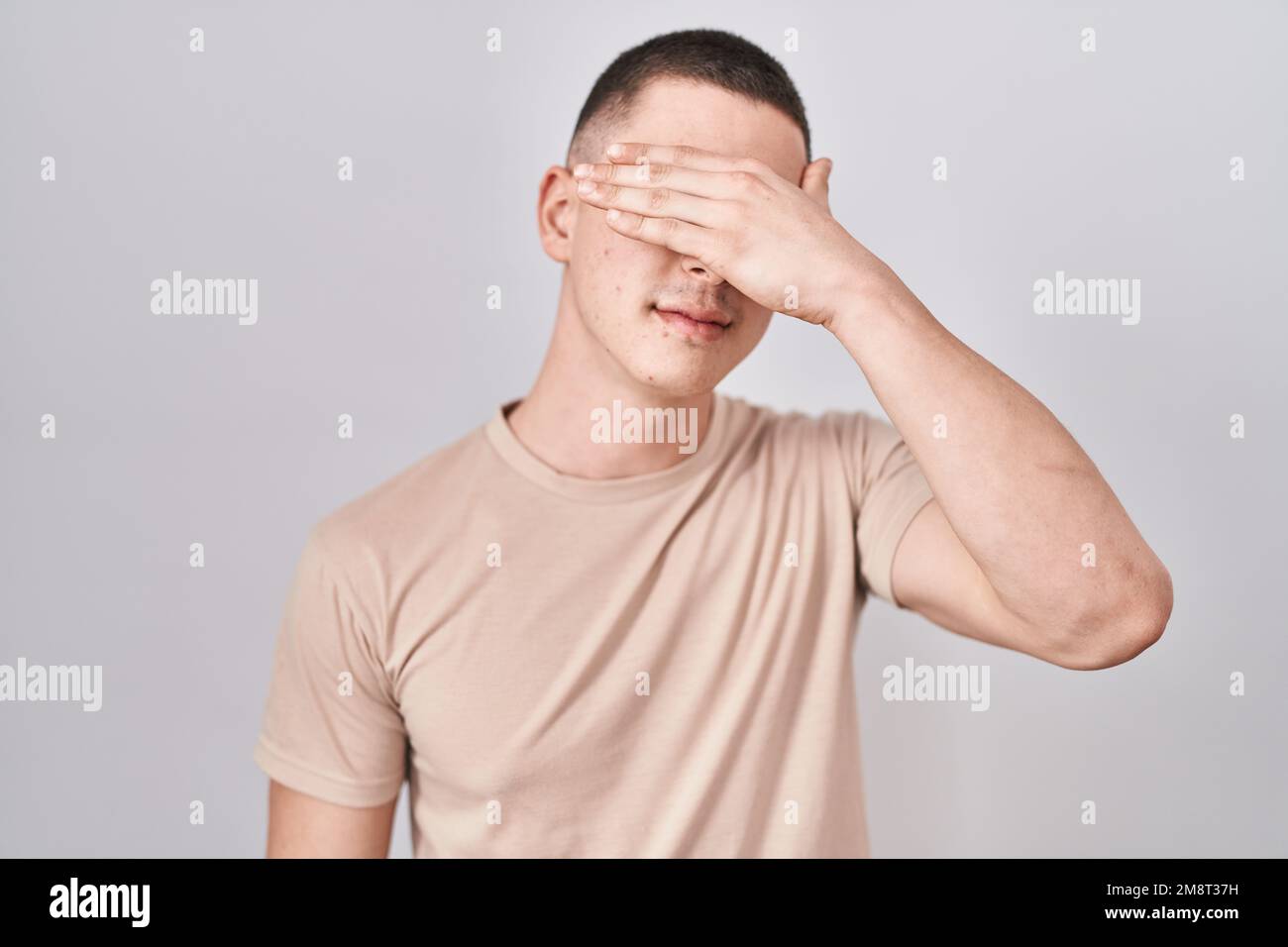 Young man standing over isolated background covering eyes with hand ...