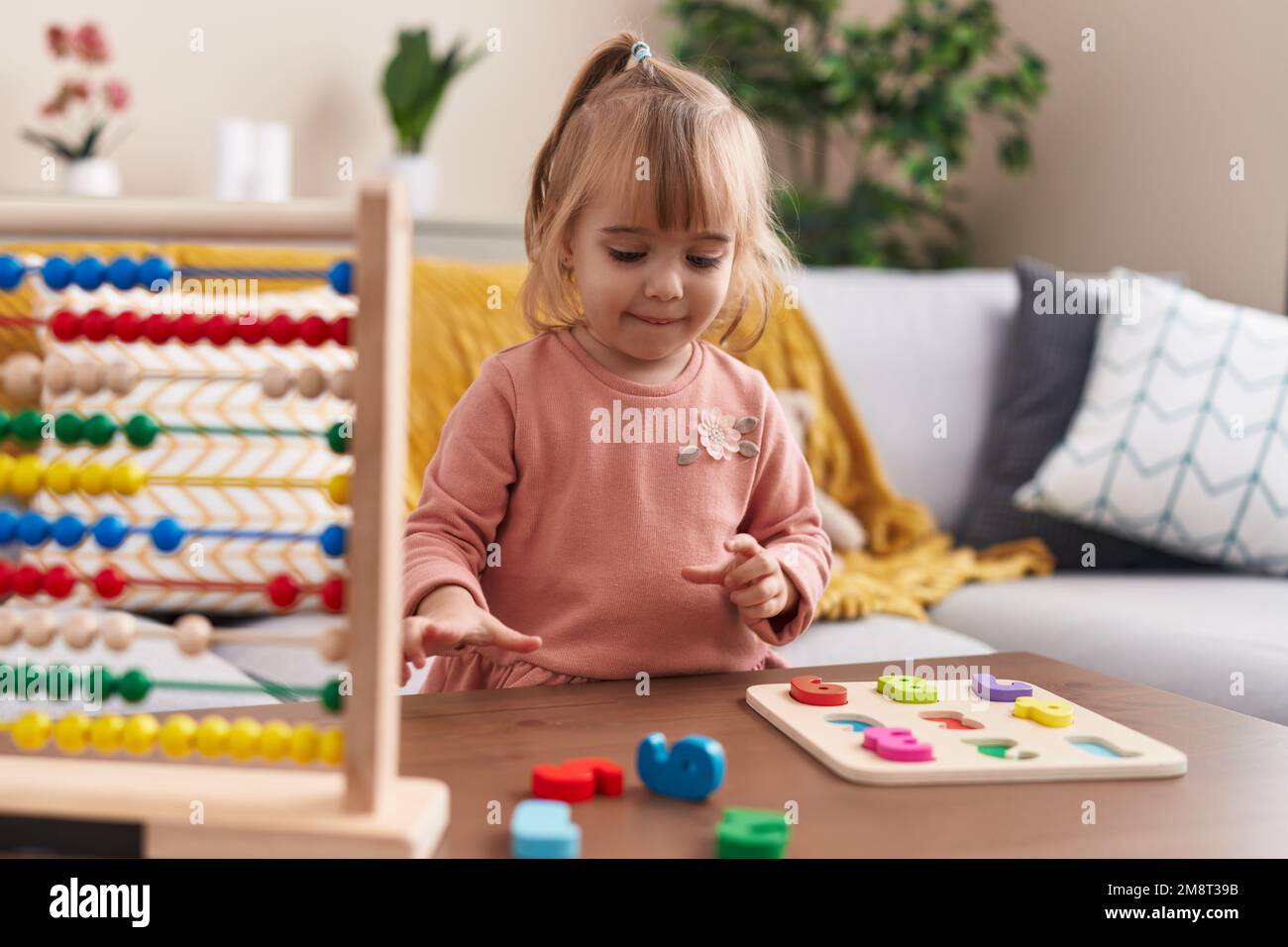 Adorable blonde girl playing maths puzzle game standing at home Stock ...