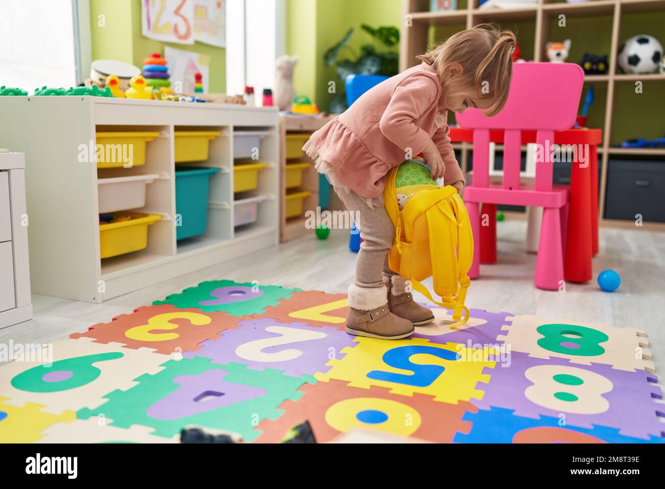 Adorable blonde girl preschool student opening backpack at kindergarten ...