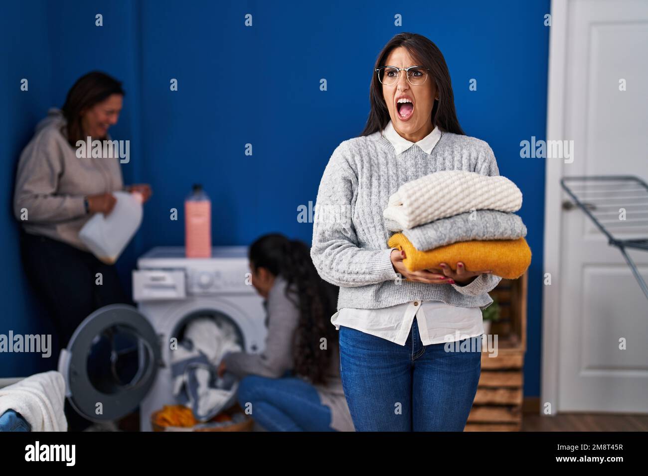 Three women doing laundry at home angry and mad screaming frustrated ...
