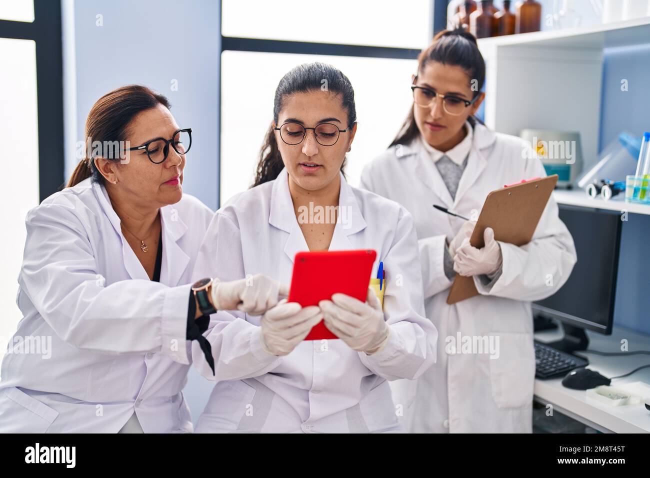 Three woman scientists using touchpad write on checklist at laboratory ...