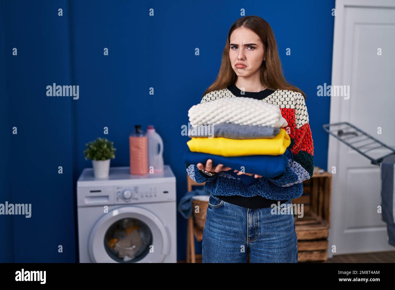 Young hispanic girl holding clean laundry depressed and worry for distress, crying angry and ...
