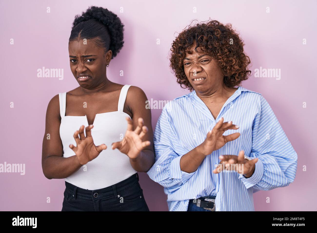 Two african women standing over pink background disgusted expression ...