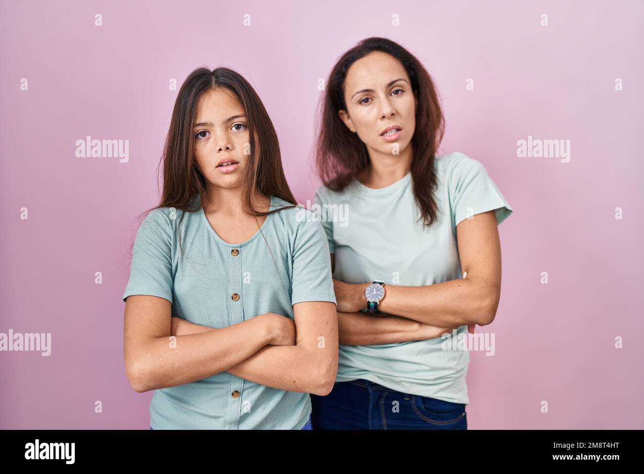 Young mother and daughter standing over pink background skeptic and ...