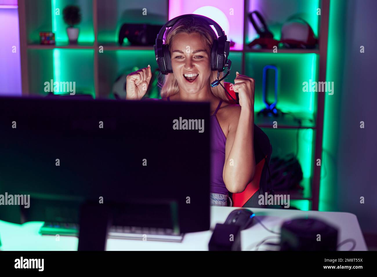 Young blonde woman streamer playing video game with winner expression ...