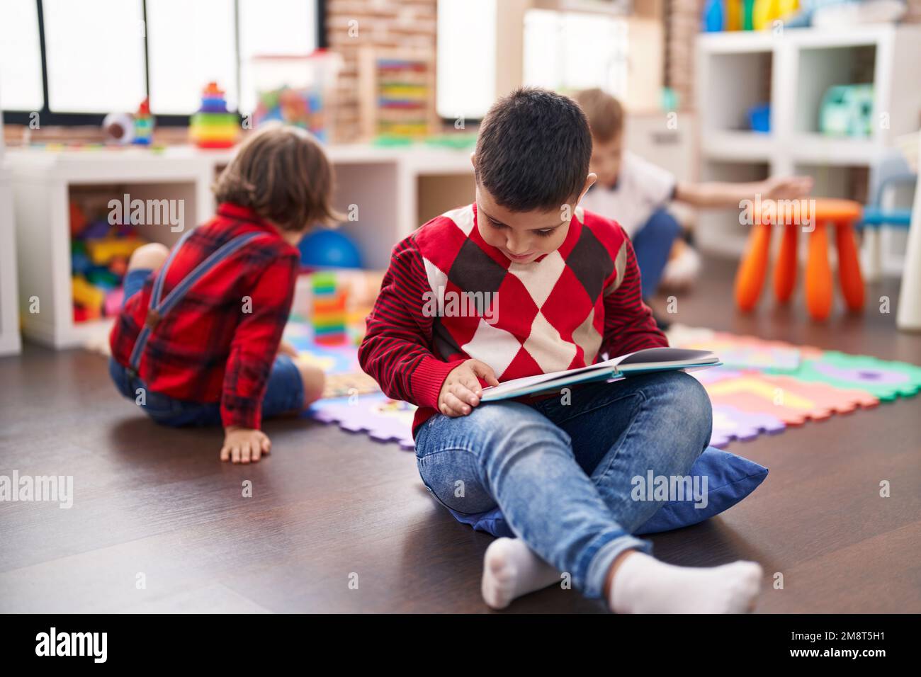 Two kids reading book sitting on floor at kindergarten Stock Photo - Alamy