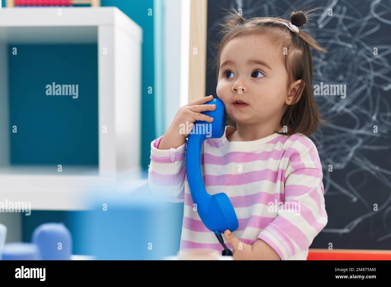 Adorable chinese toddler playing telephone toy standing at kindergarten ...