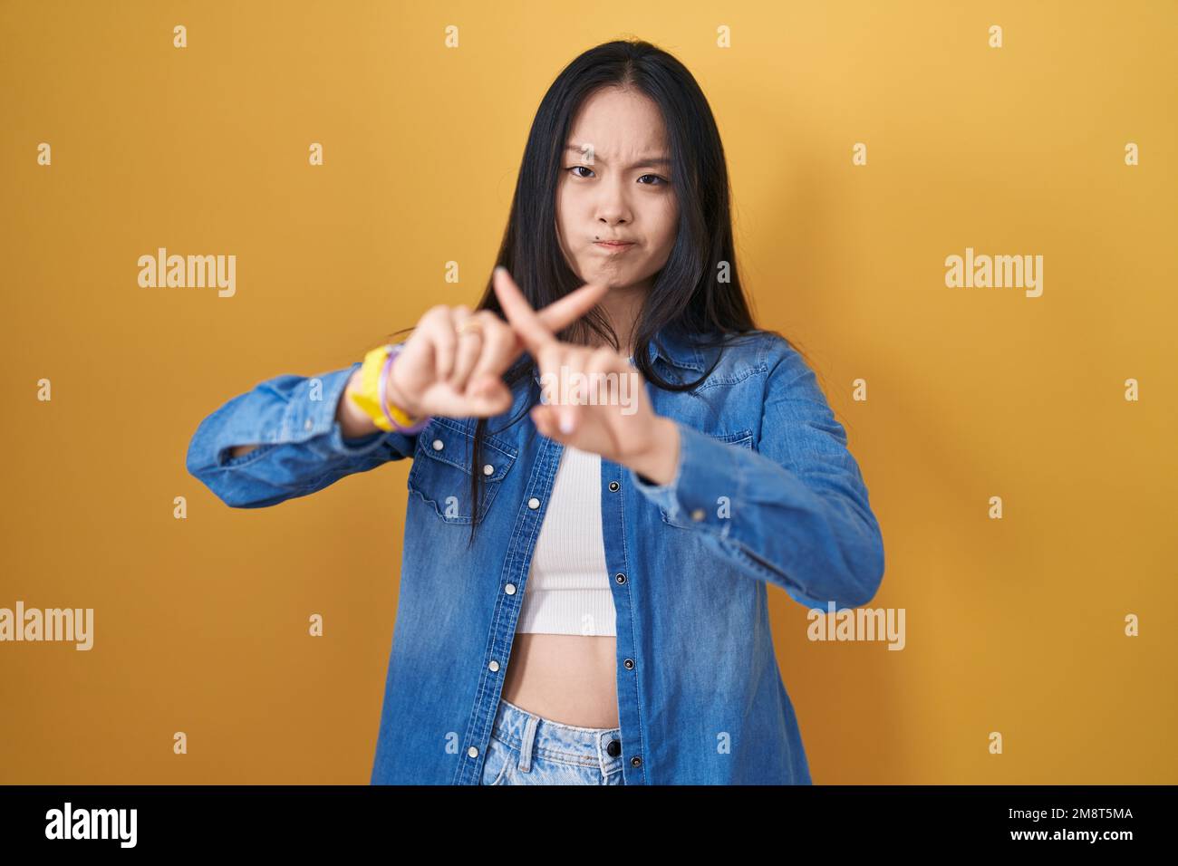 Young asian woman standing over yellow background rejection expression ...