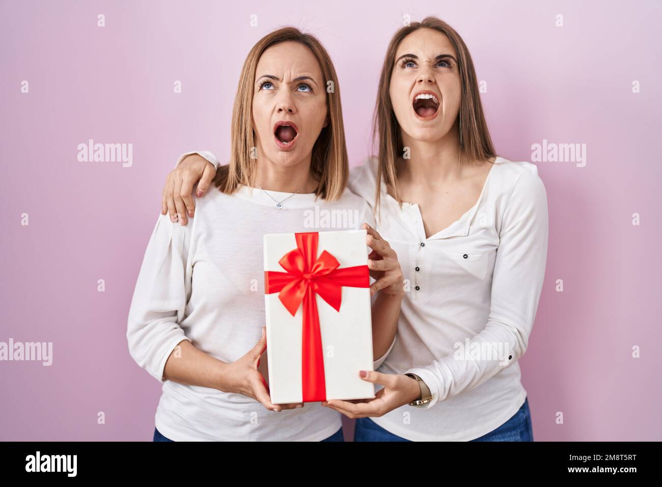 Middle age mother and young daughter holding mothers day gift angry and ...
