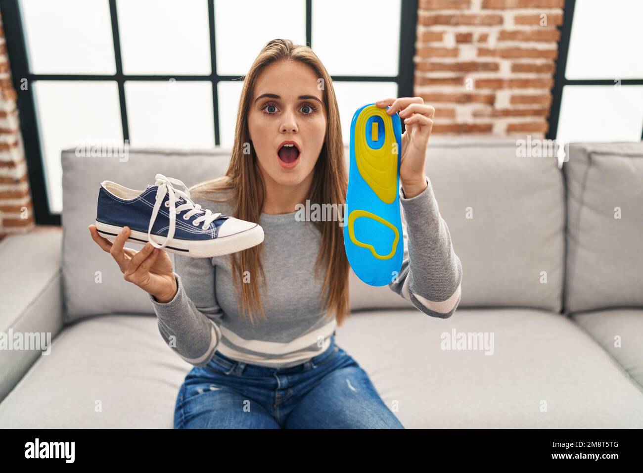 Young woman holding shoe insole afraid and shocked with surprise and ...