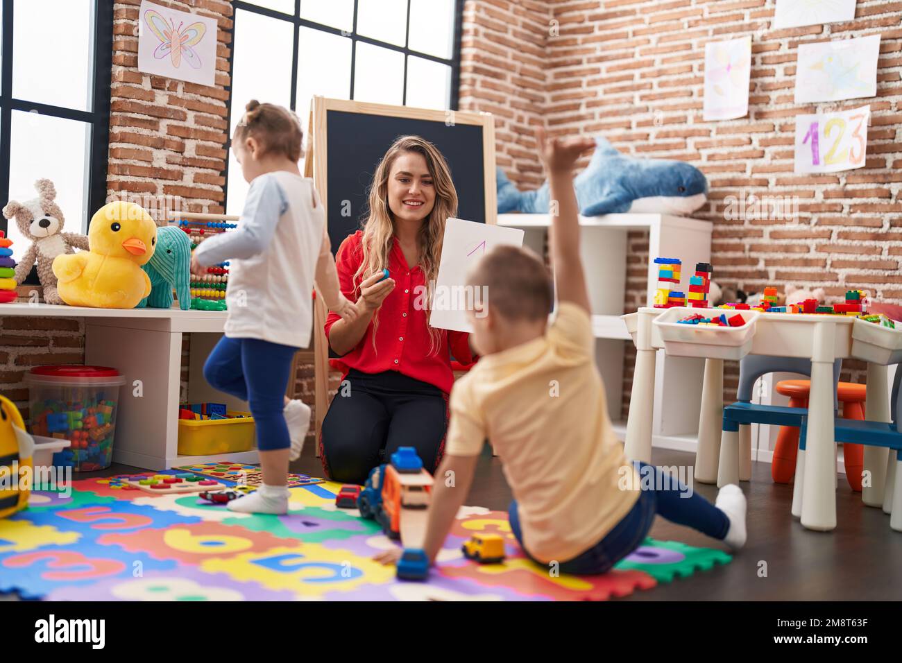 Teacher with boy and girl sitting on floor having maths lesson at ...