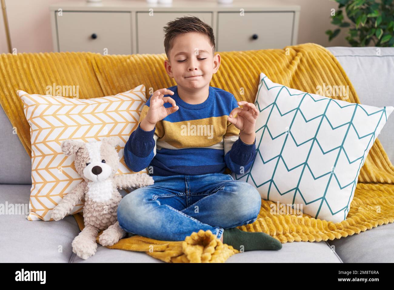 Adorable hispanic boy doing yoga exercise sitting on sofa at home Stock ...