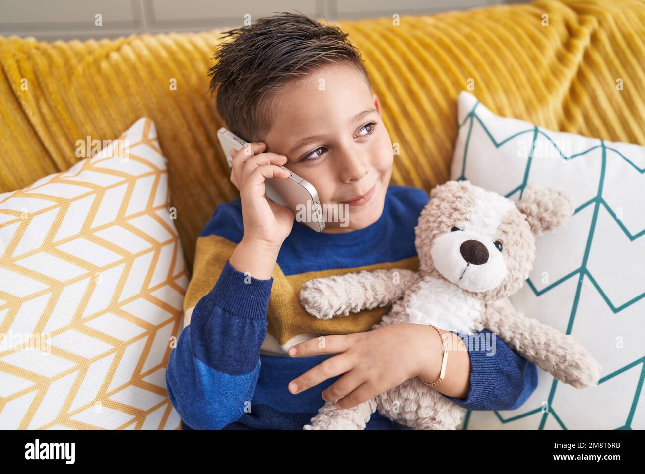 Adorable hispanic boy hugging teddy bear talking on smartphone at home ...