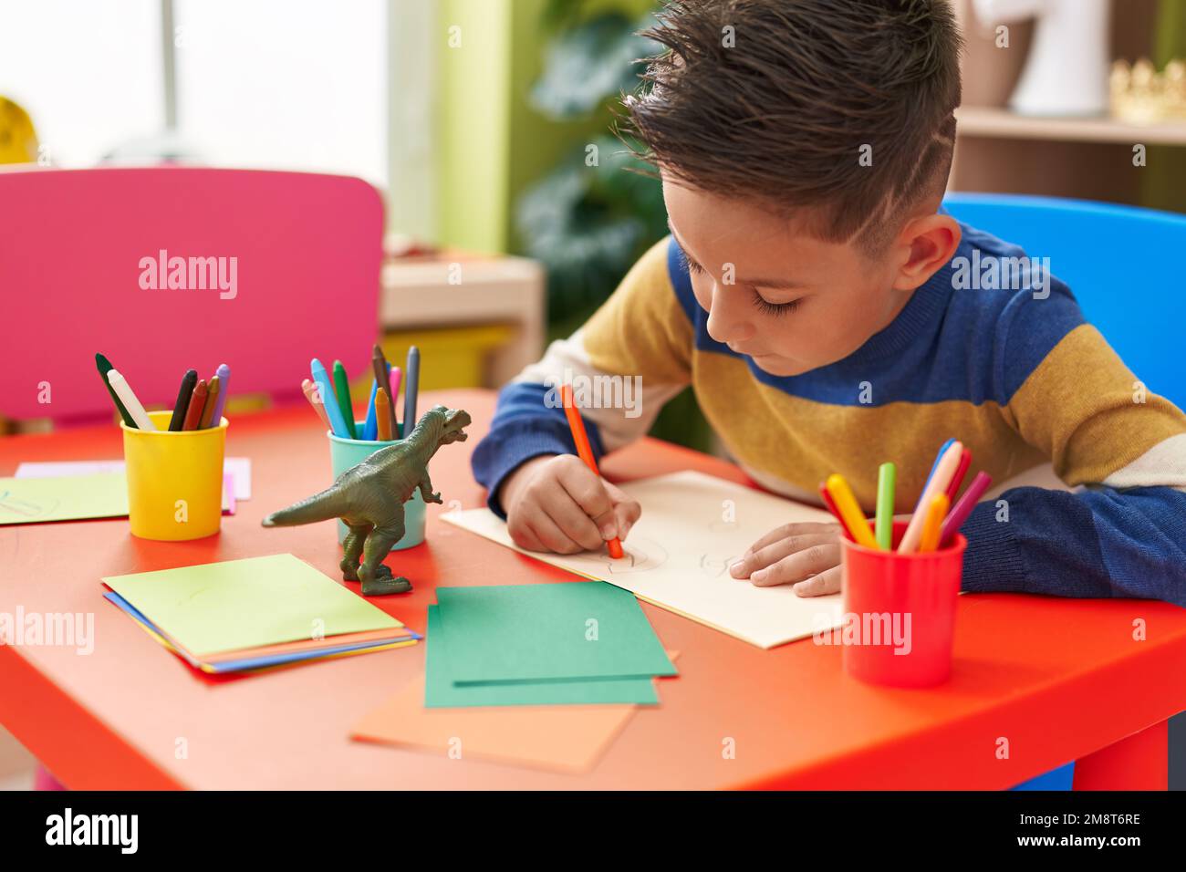 Adorable hispanic boy preschool student sitting on table drawing on ...