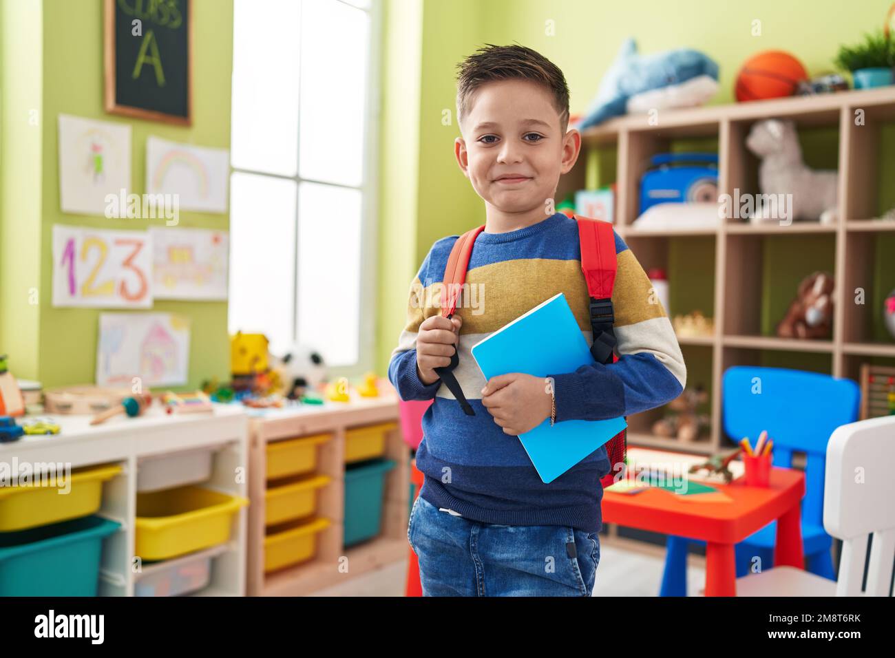 Adorable hispanic boy student wearing backpack holding book at ...