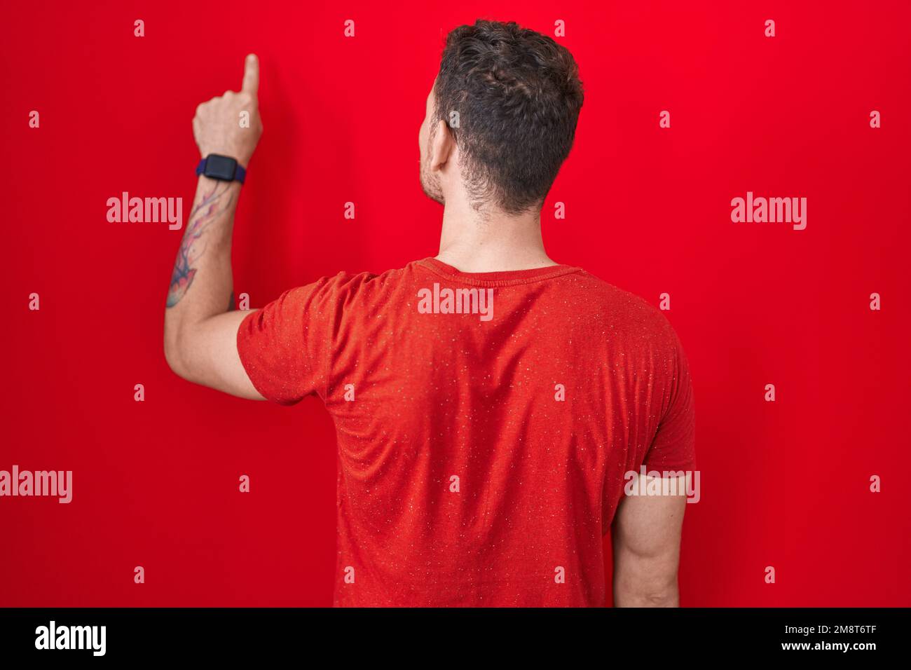 Young hispanic man standing over red background posing backwards ...