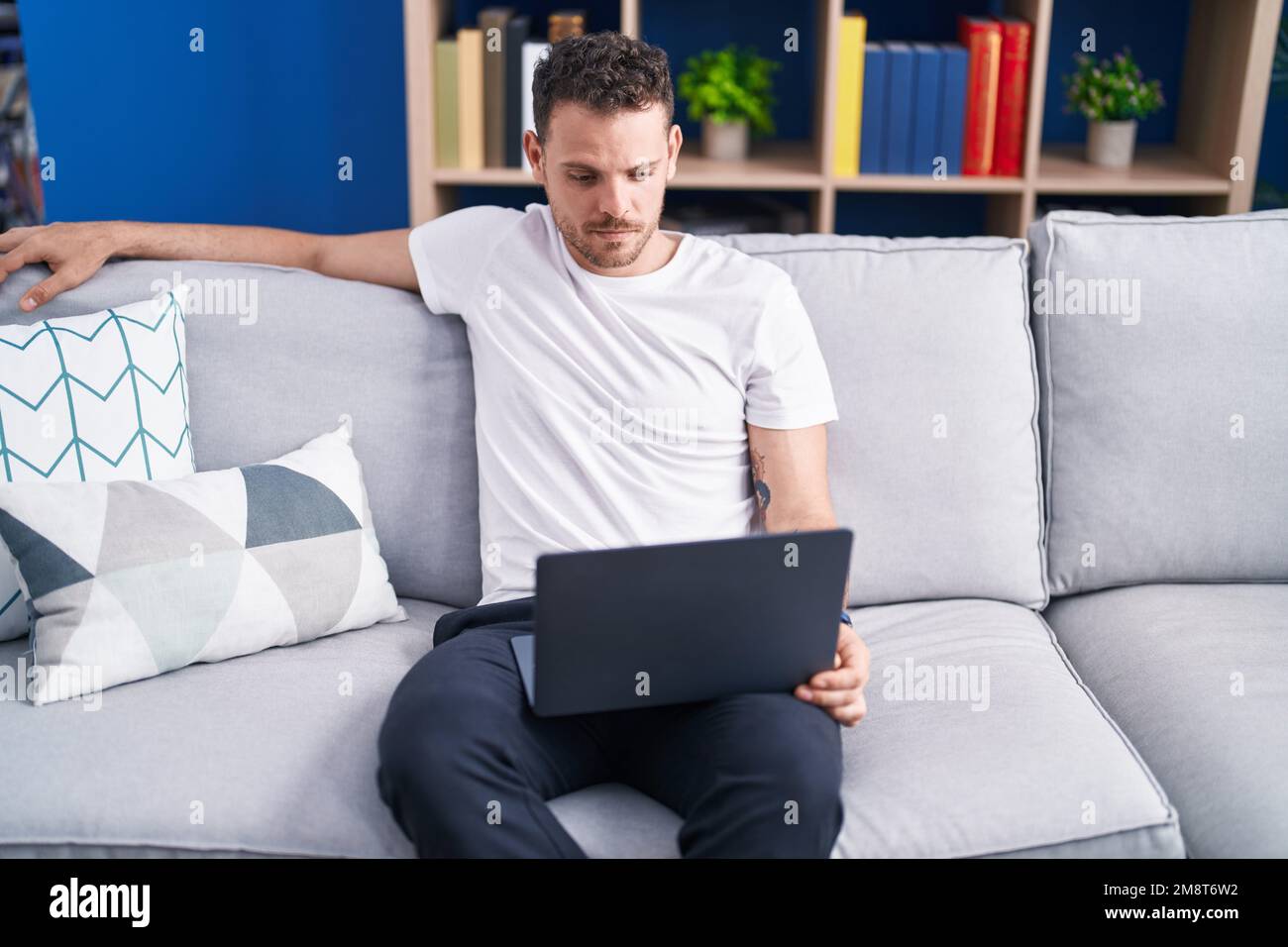Young hispanic man using laptop sitting on sofa at home Stock Photo - Alamy