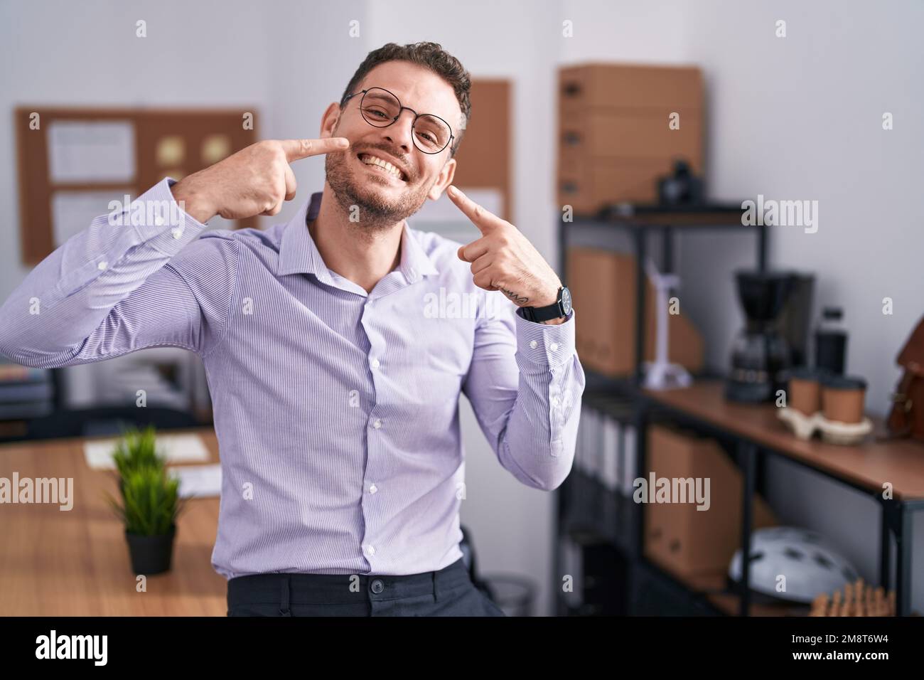 Young hispanic man at the office smiling cheerful showing and pointing ...
