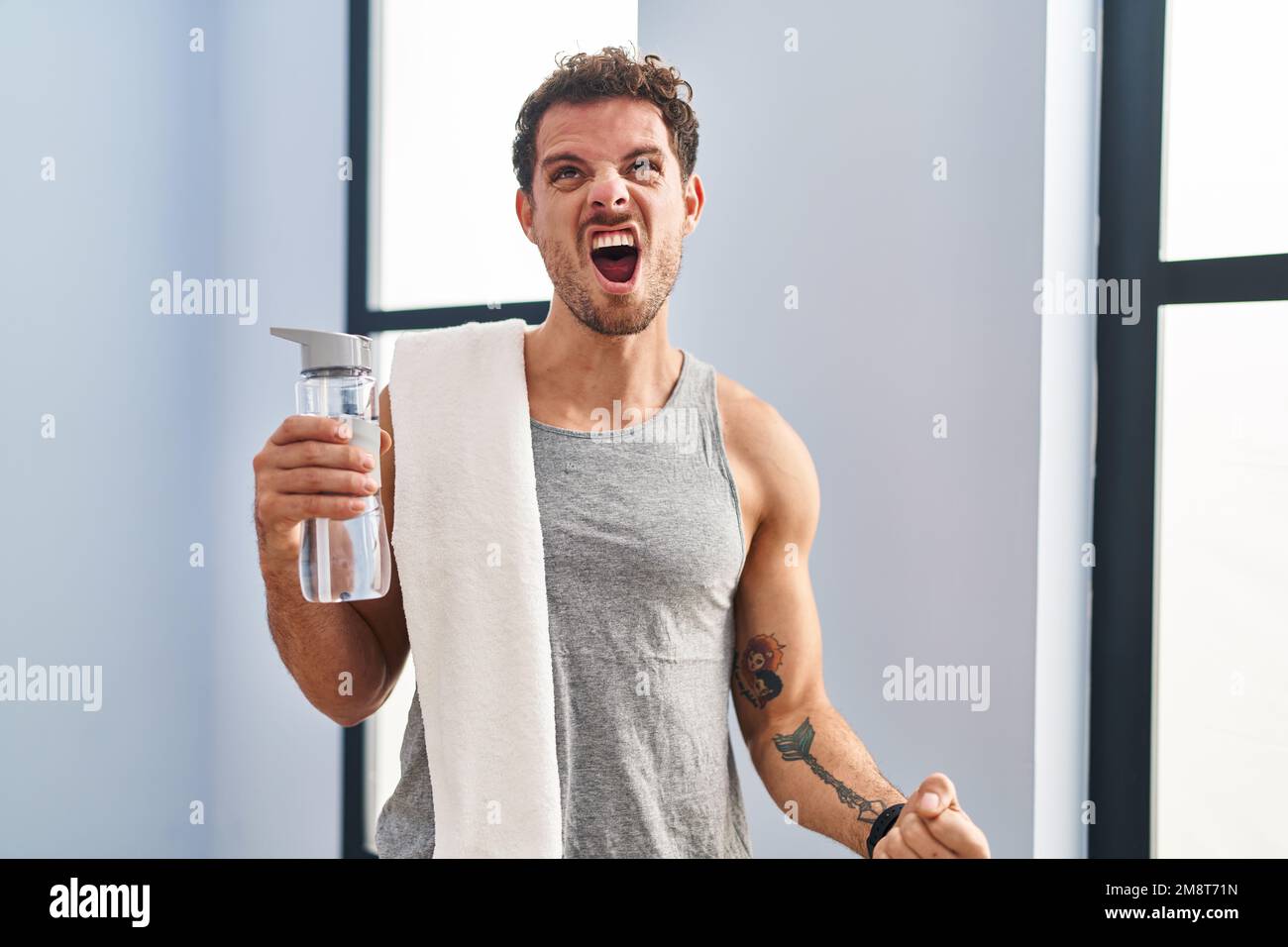Young hispanic man wearing sportswear drinking water angry and mad ...