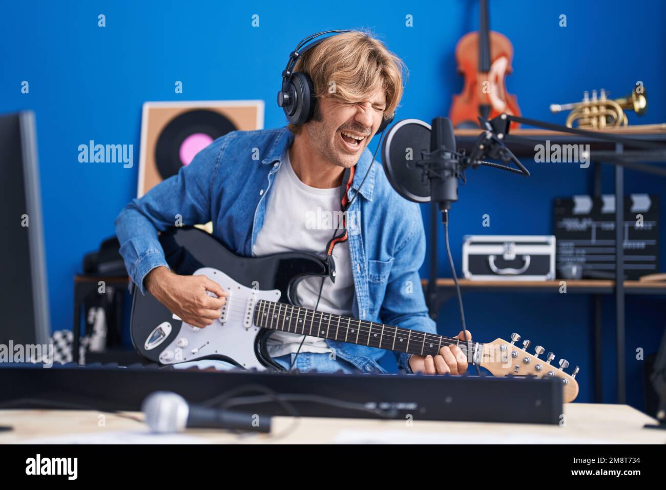 Young man artist singing song playing electrical guitar at music studio ...