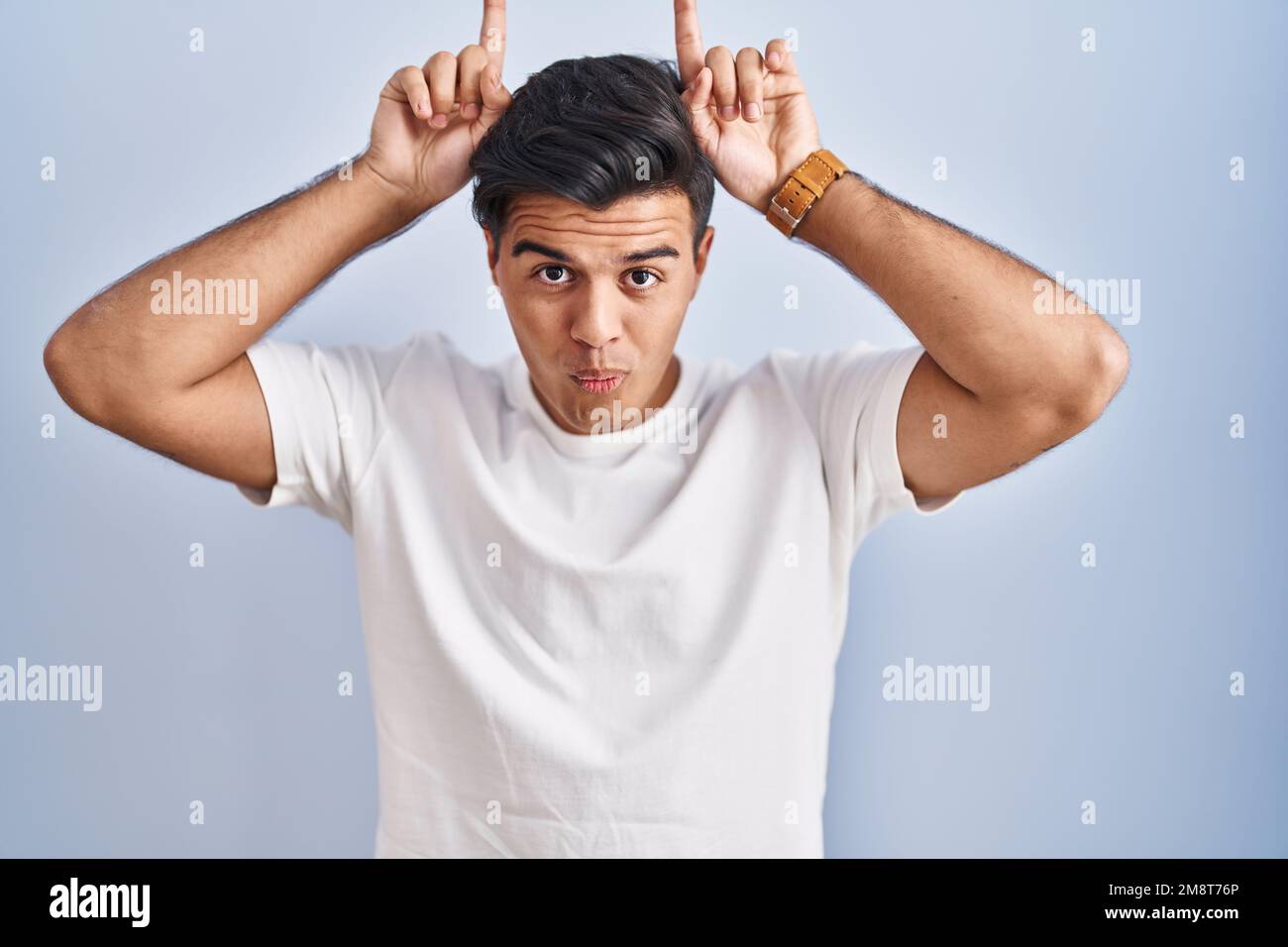 Hispanic man standing over blue background doing funny gesture with ...
