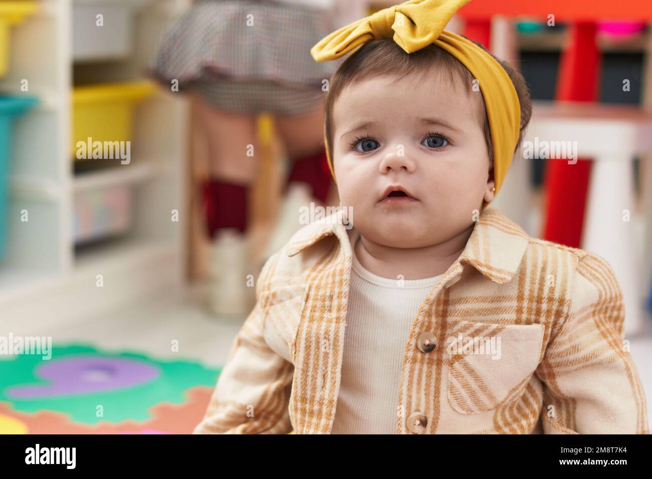 Adorable blonde toddler sitting on floor with serious expression at ...