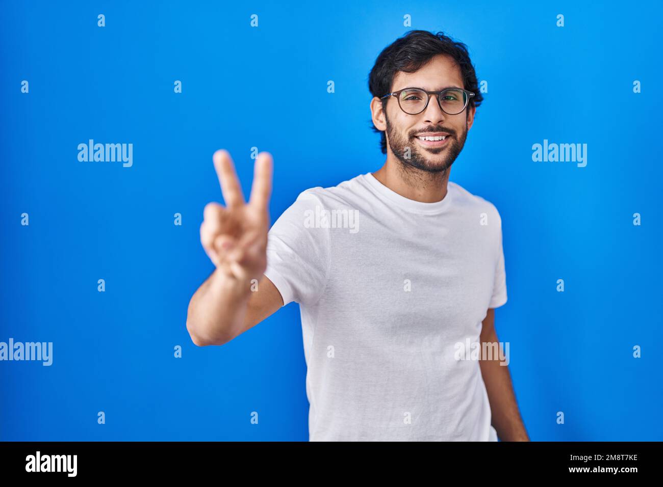 Handsome latin man standing over blue background smiling looking to the ...