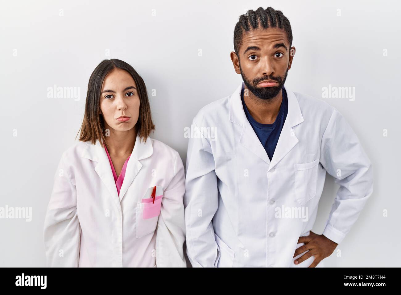 Young hispanic doctors standing over white background depressed and ...